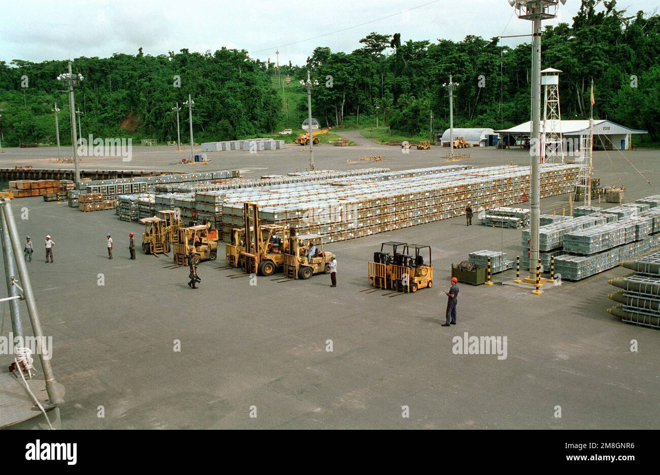 Containers of ordnance line a pier as forklifts stand by to load the ...