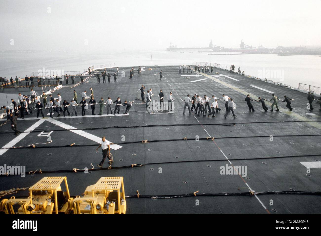 Crewmen pull deperming coils across the flight deck of the amphibious ...