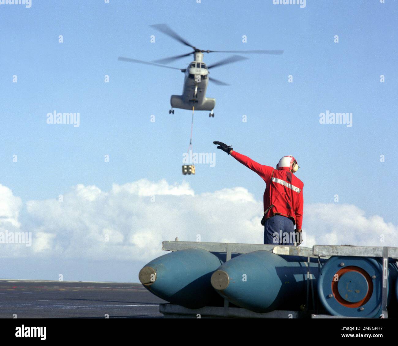 A flight deck control officer signals to a CH-46 Sea Knight helicopter ...
