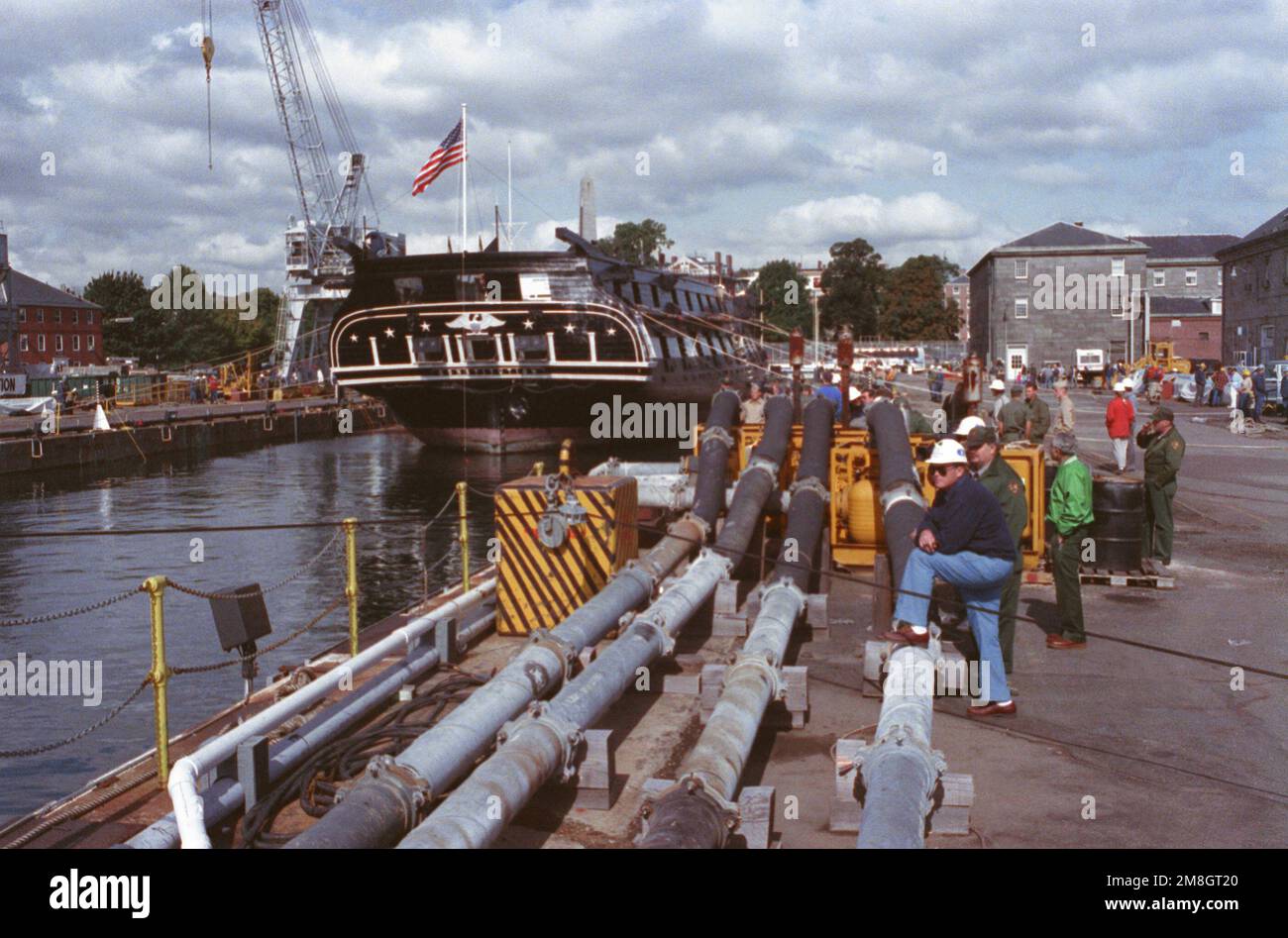 Workers wait as water is pumped from the dry dock holding the 44-gun ...