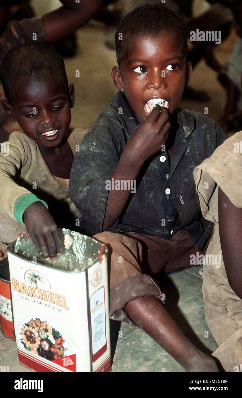 Two Somalian children sit on the floor eating Maizemeal provided by the ...