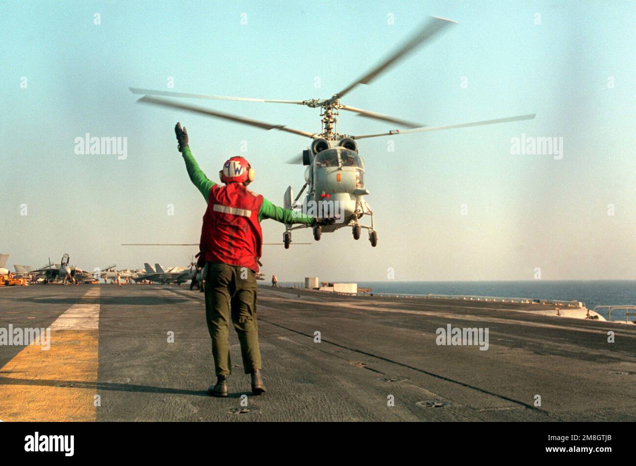 A flight deck crew member signals to the pilot of a Ka-27 Helix ...