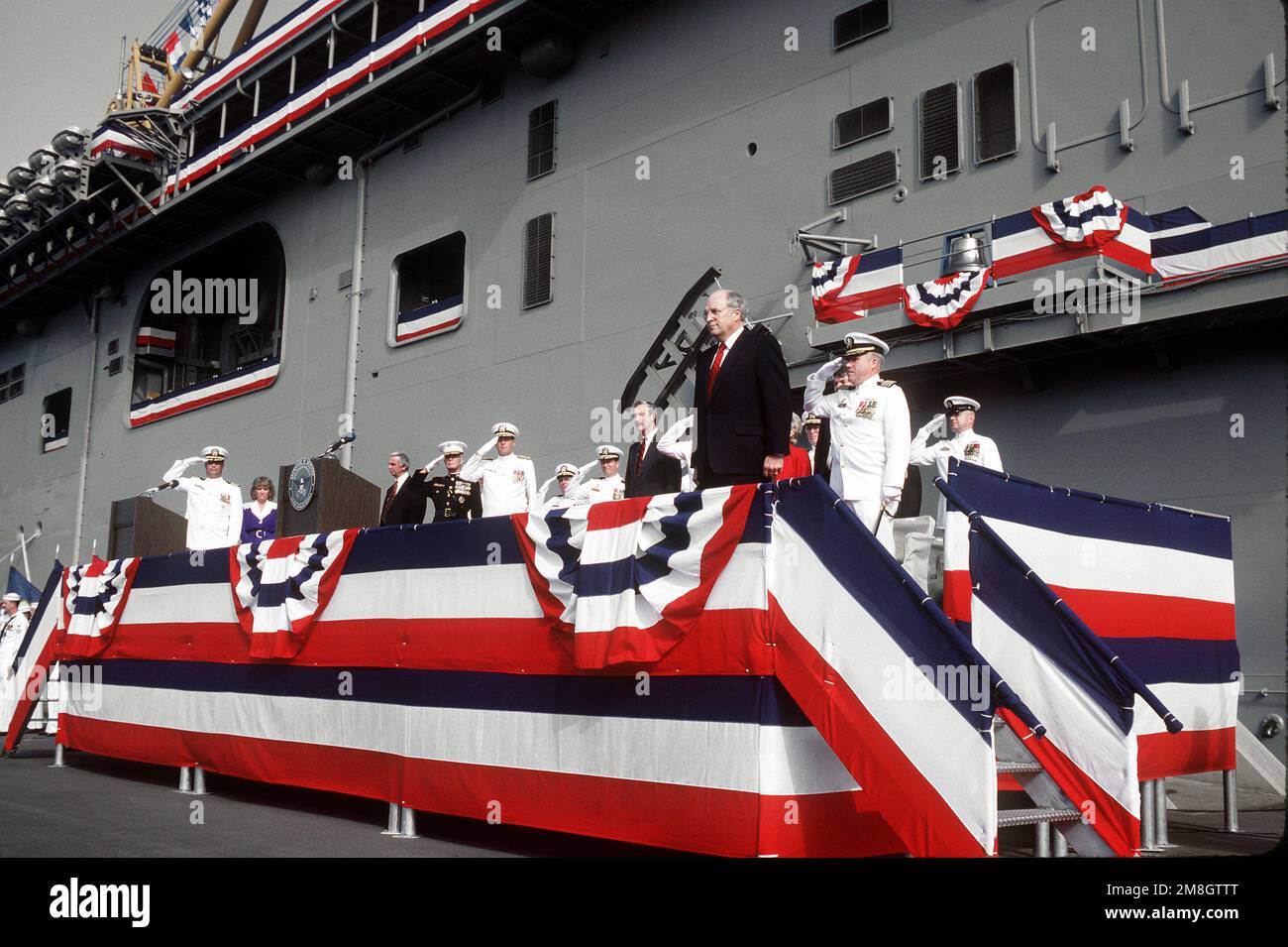 Naval officers salute and civilian dignitaries stand at attention ...