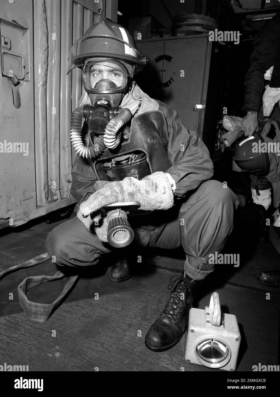 A crewman wearing oxygen breathing apparatus aims the nozzle of a water ...