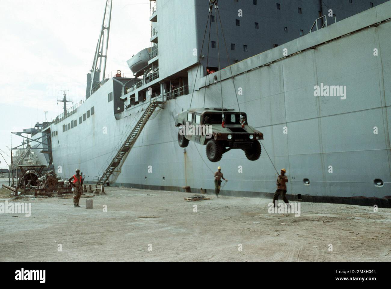 U. S. Army stevedores guide an M-998 series vehicle as it is lowered ...