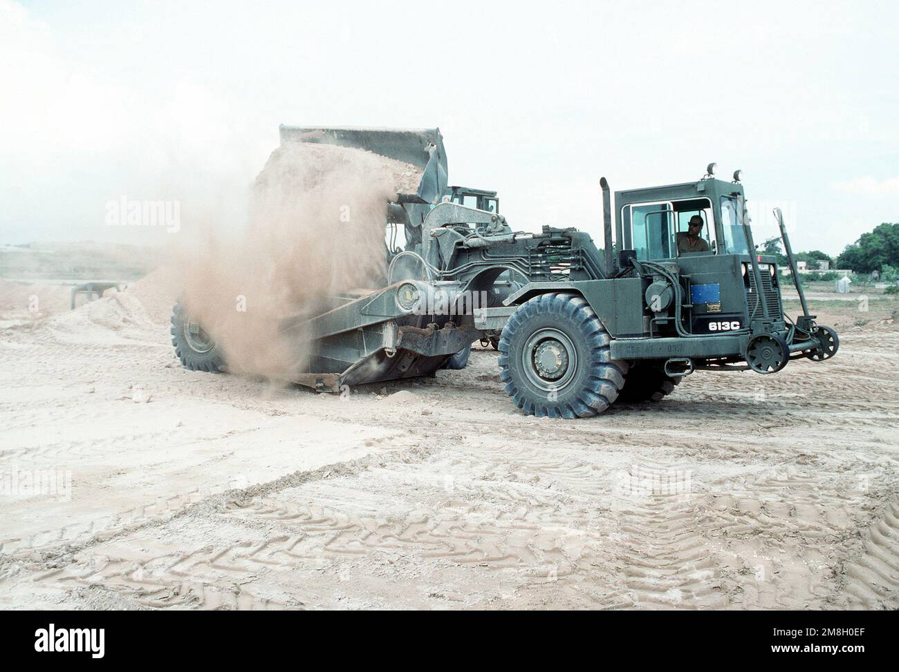 A front-end loader drops a bucket of crushed coral into an earth-mover ...