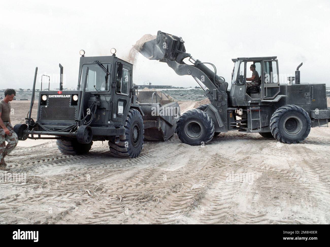 A front-end loader drops a bucket of crushed coral into an earth-mover ...
