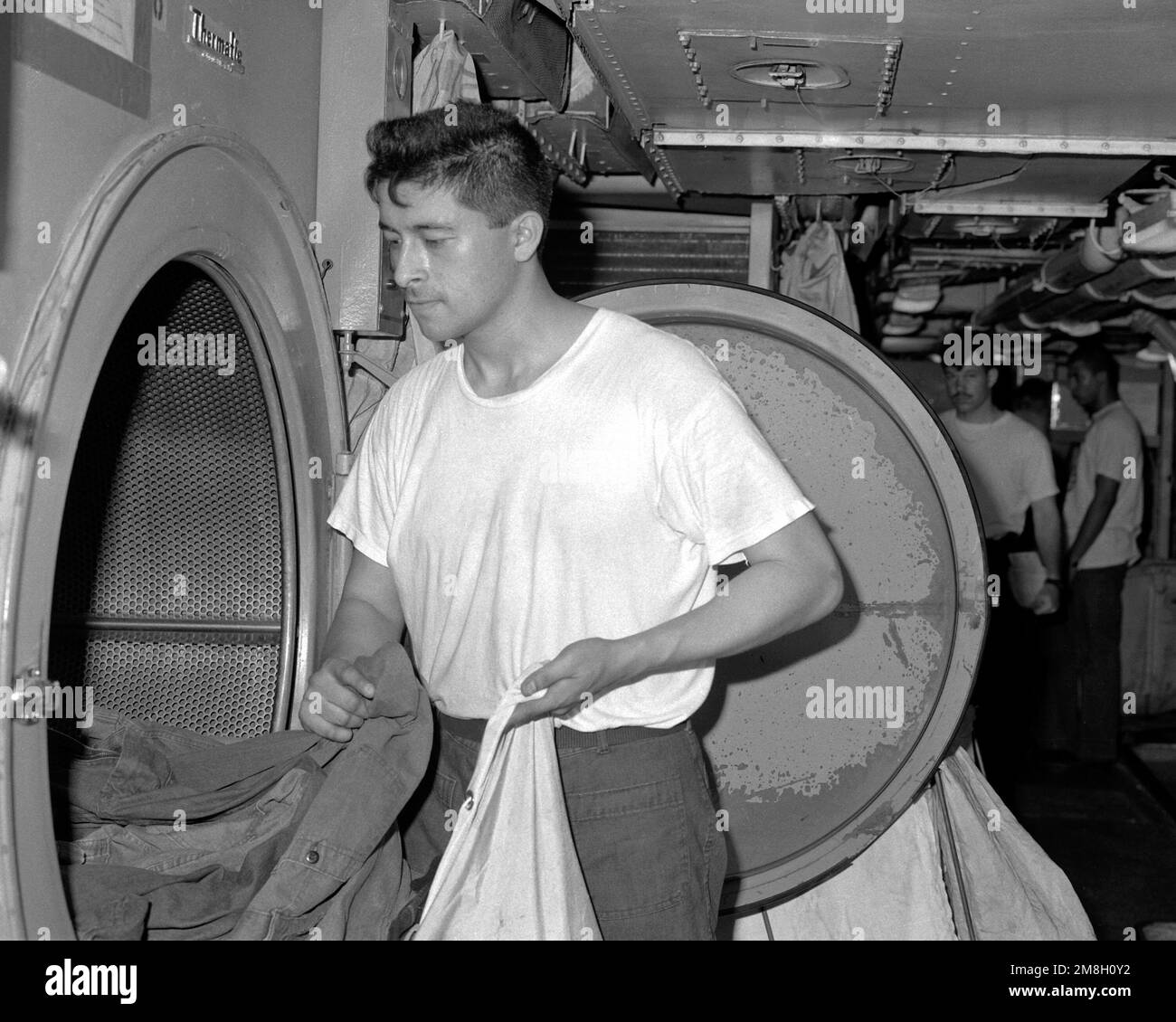 SEAMAN Danny Diaz removes clothes from a dryer in the ship's laundry ...