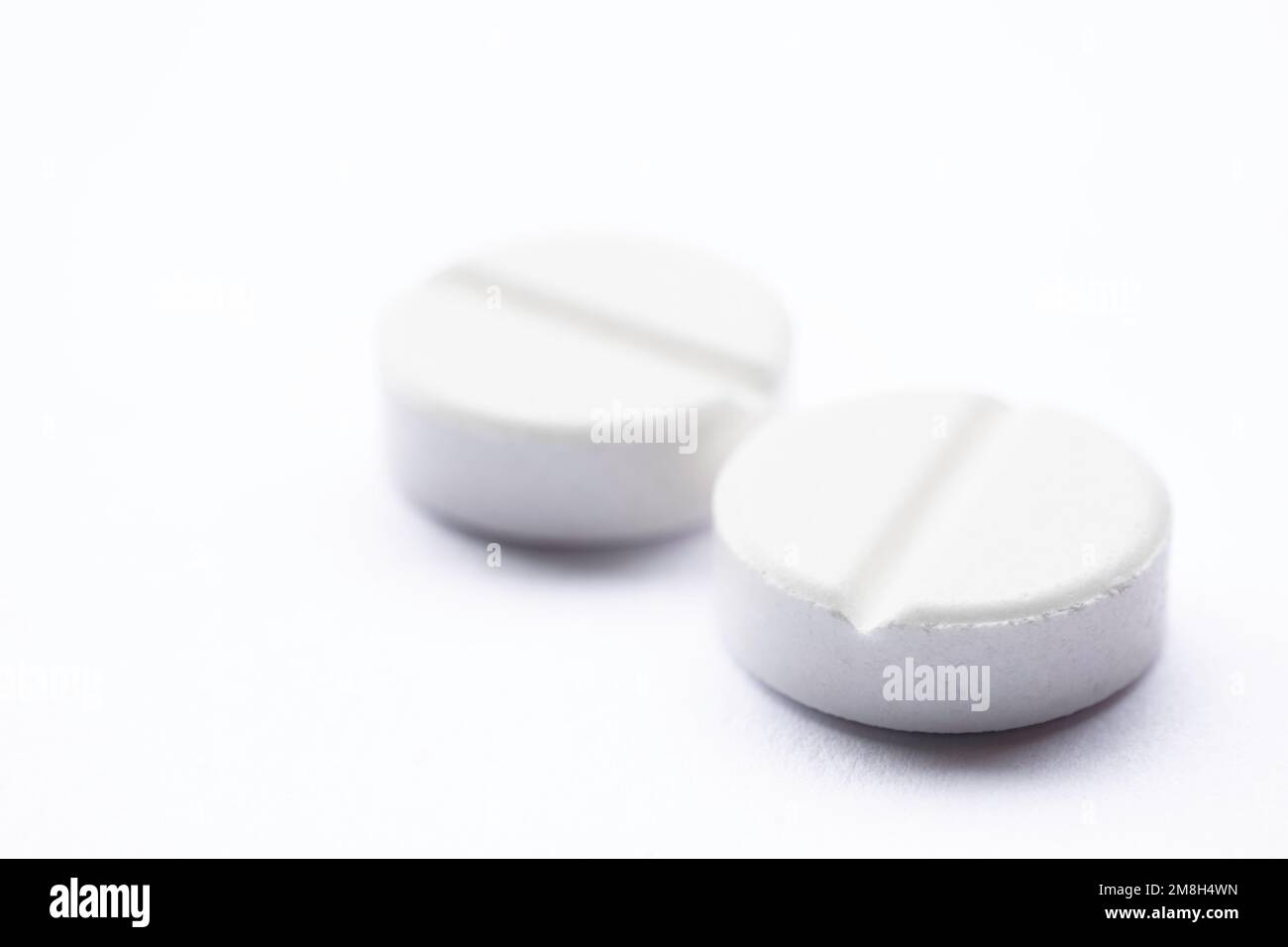 Two medicine tablets with score line on a white background. Narrow ...