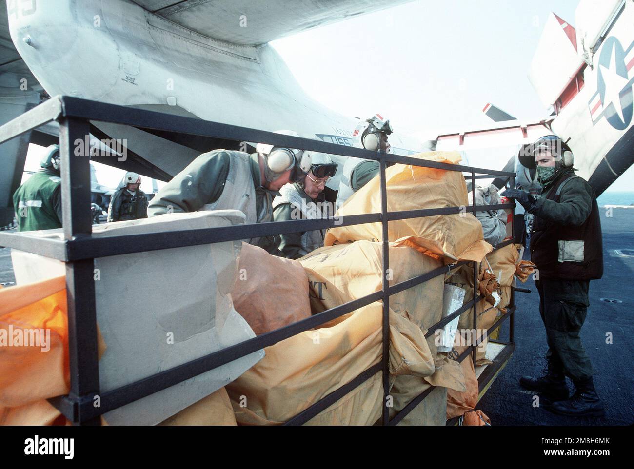 Flight deck personnel stack bags of mail being unloaded from a Fleet ...