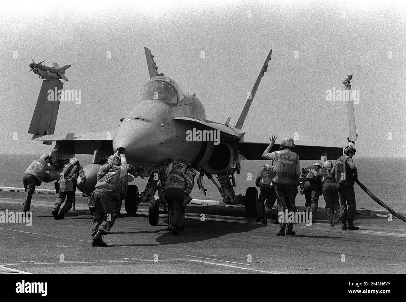 Flight deck crew members push an F/A-18C Hornet aircraft into a parking ...