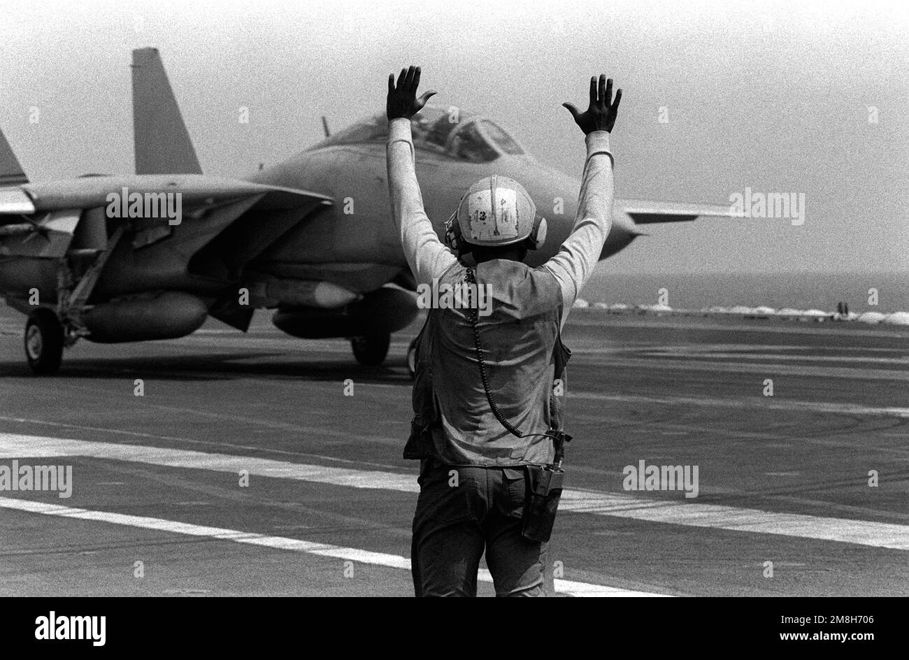 A flight deck crew member signals to the pilot of an F-14A Tomcat ...