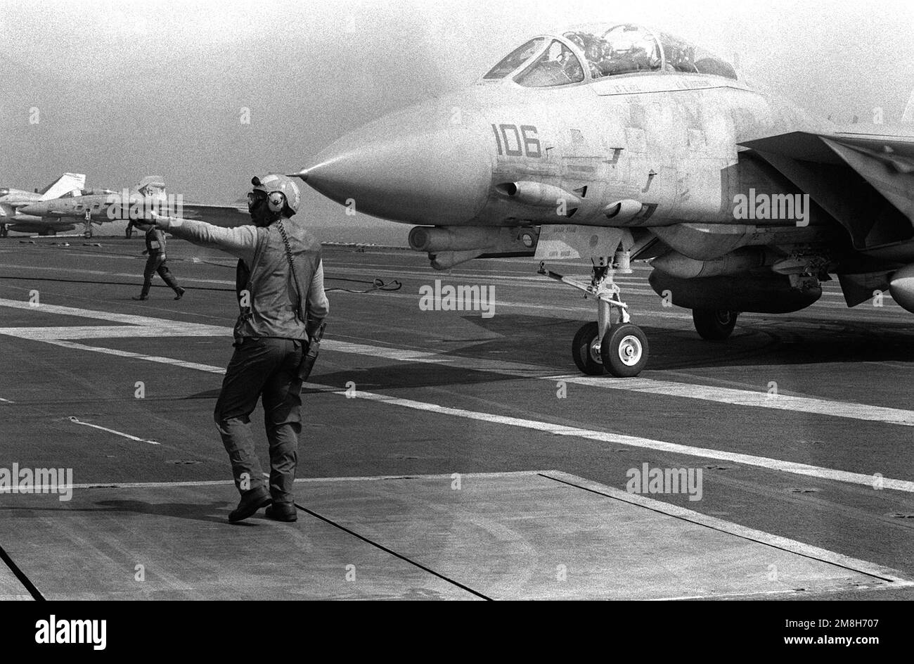 A flight deck crew member signals to the pilot of an F-14A Tomcat ...