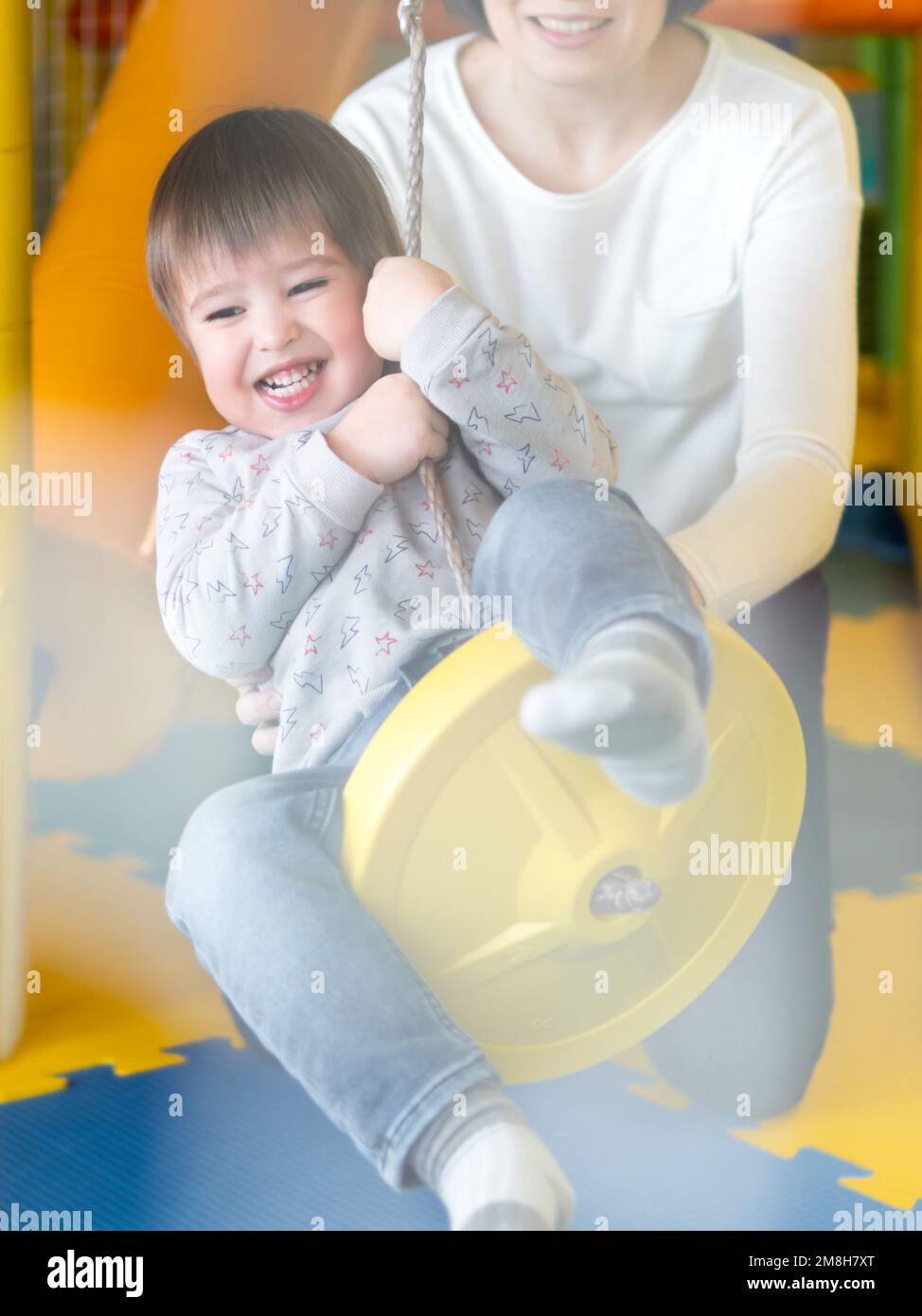 Toddler plays on rope swing with his mother or babysitter. Physical ...