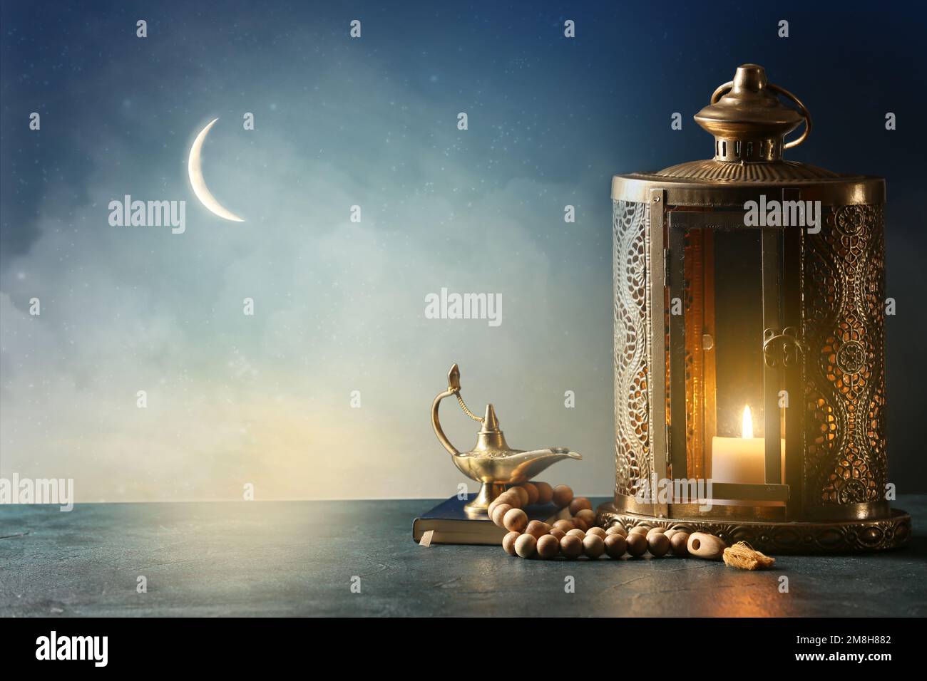 Muslim lantern with Quran, Aladdin lamp and tasbih on table at night ...