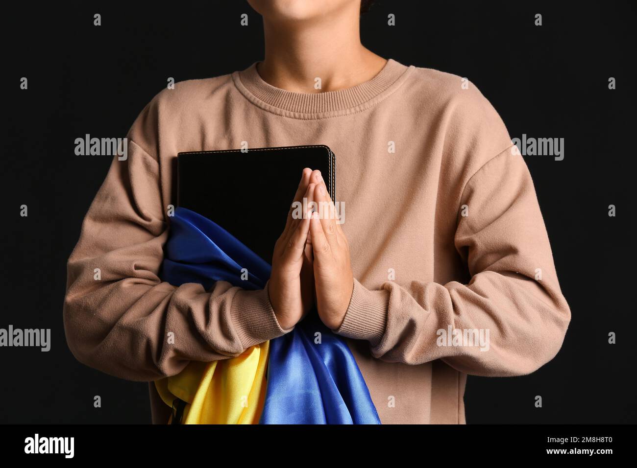 Little boy with Holy Bible and flag of Ukraine praying on black ...