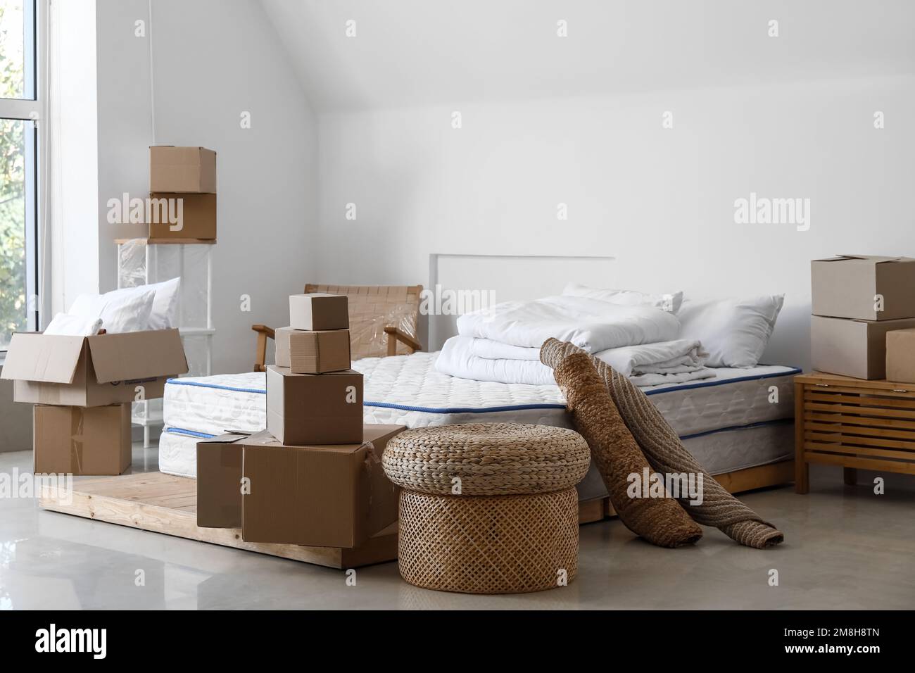 Cardboard boxes with bed, poufs and rolled carpets in bedroom on moving ...