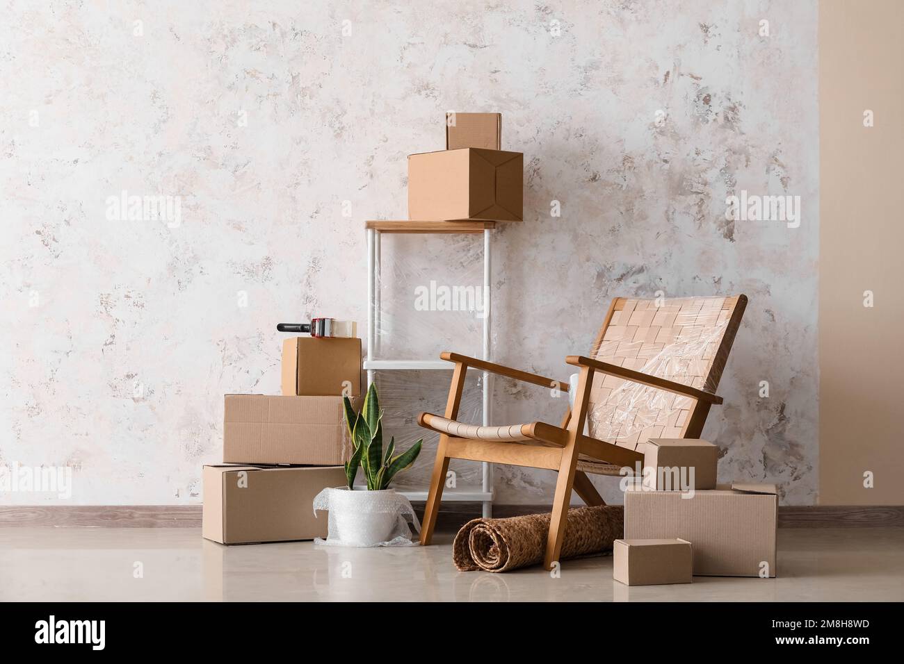 Moving cardboard boxes with armchair, houseplant, rolled carpet and ...