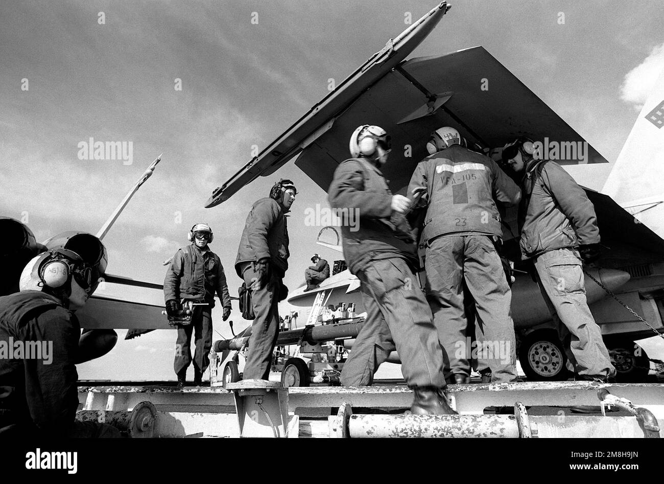 Flight deck crew members check beneath the wing of a Strike Fighter ...