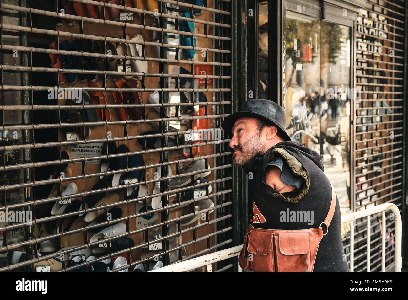A one-armed man with a hat looking at a shoe store through some ...