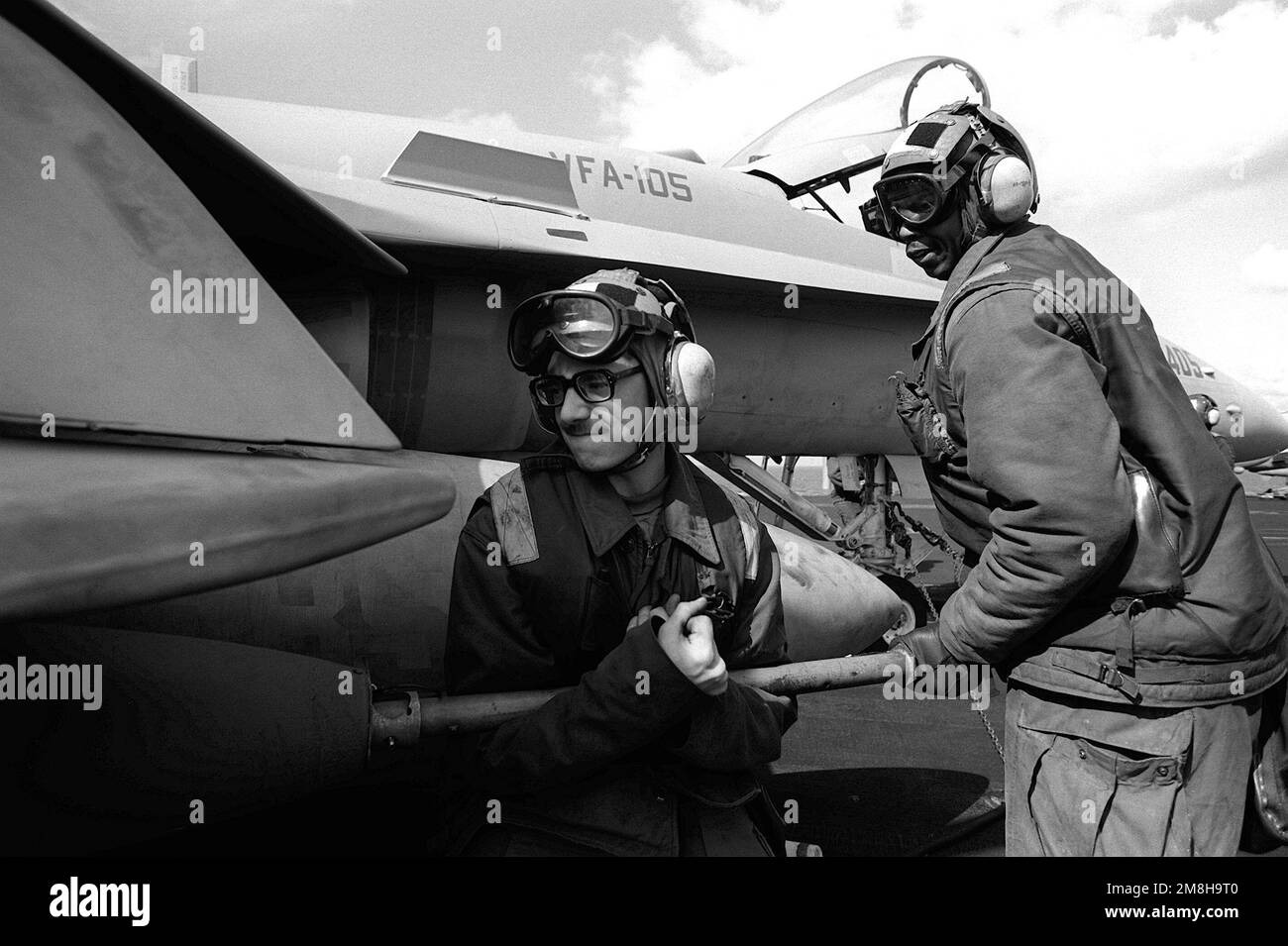 Aviation ordnancemen position a 500-pound practice bomb on a wing pylon ...