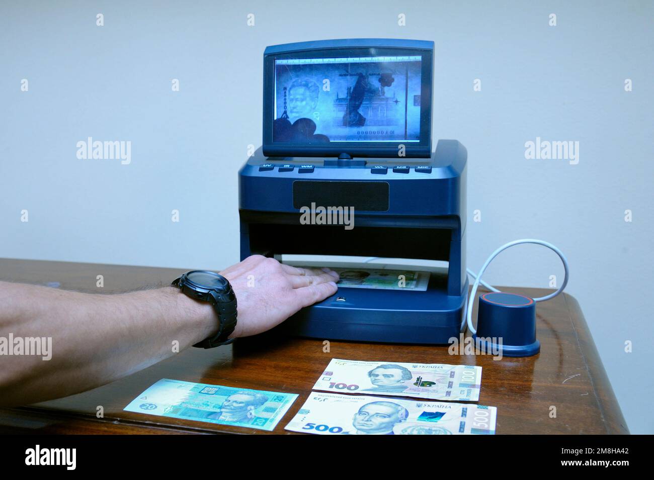 Man hand switching money detector on, banknote placed in receiver. Kyiv ...