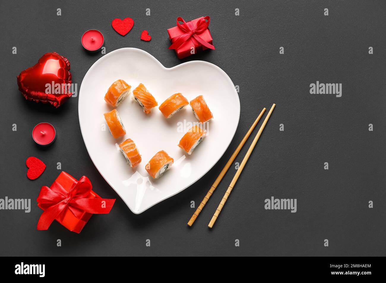 Plate with sushi rolls, chopsticks, gifts and decor on black background ...
