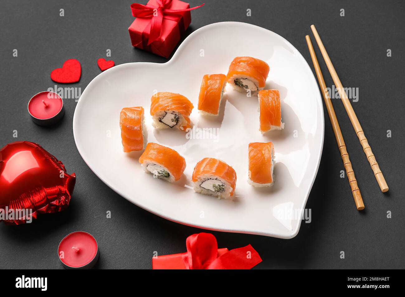 Plate with sushi rolls, chopsticks, gifts and decor on black background ...