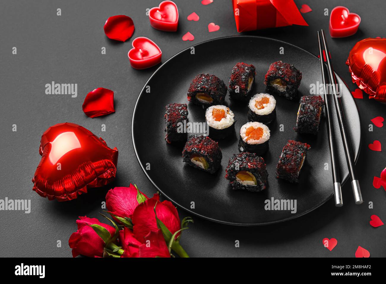 Plate with sushi rolls, chopsticks, roses and decor on black background ...