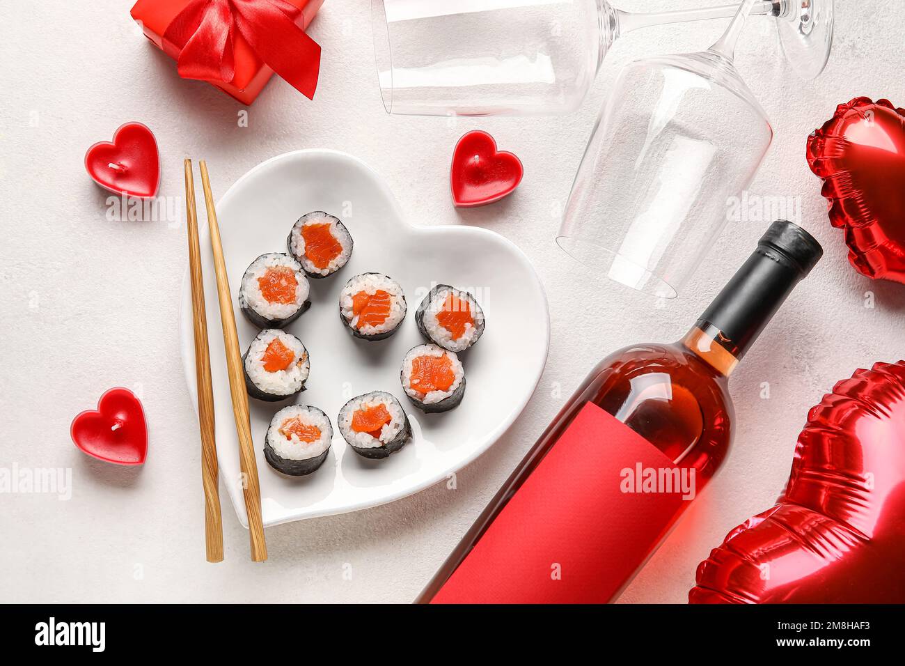 Plate with sushi rolls, chopsticks, candles, wine and gift on white ...