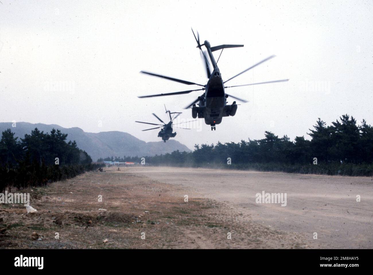 Two U.S. Marine Corps CH-53E Super Stallion helicopters lift off a dirt ...