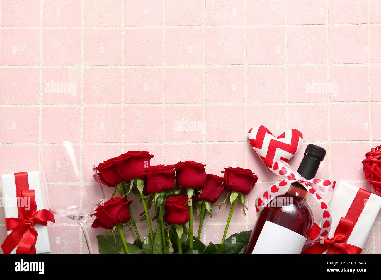 Bottle of wine rose flowers and gifts on pink tile table. Valentine's ...