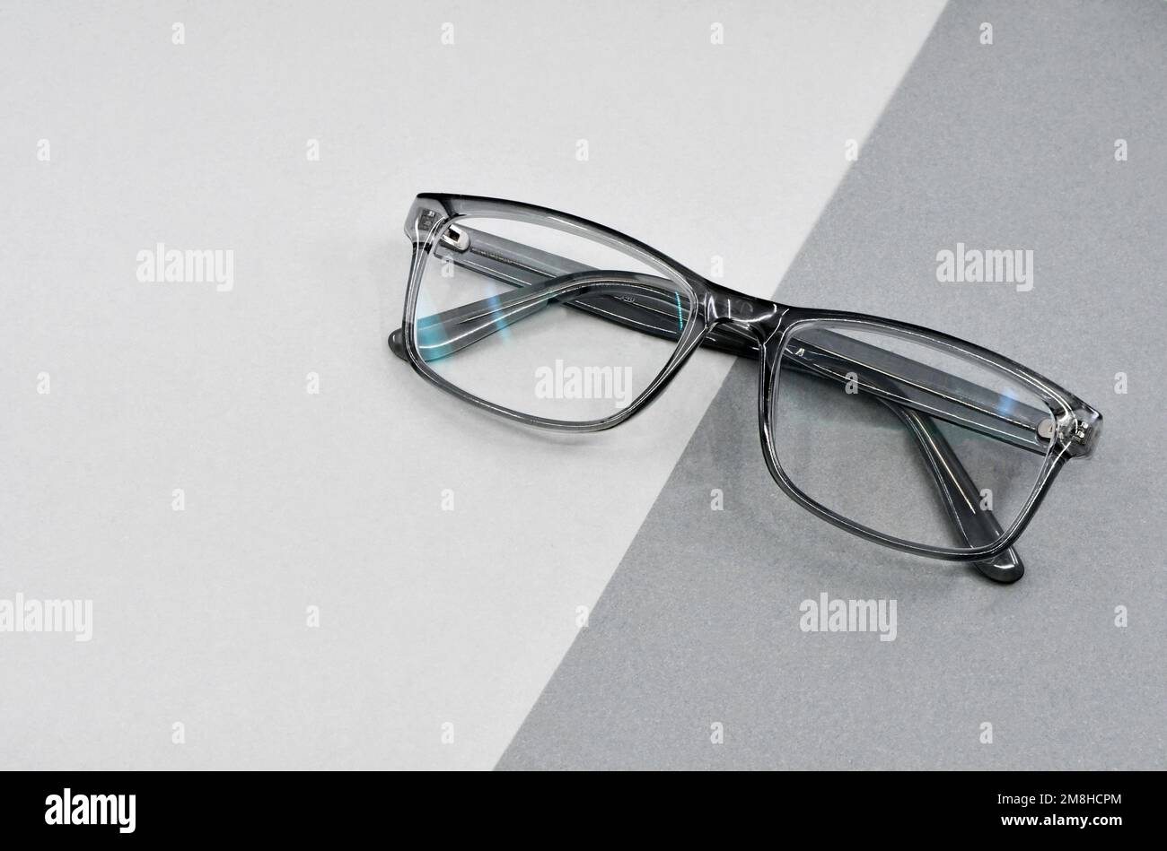 Pair of grey framed glasses on a split background of dark and light ...