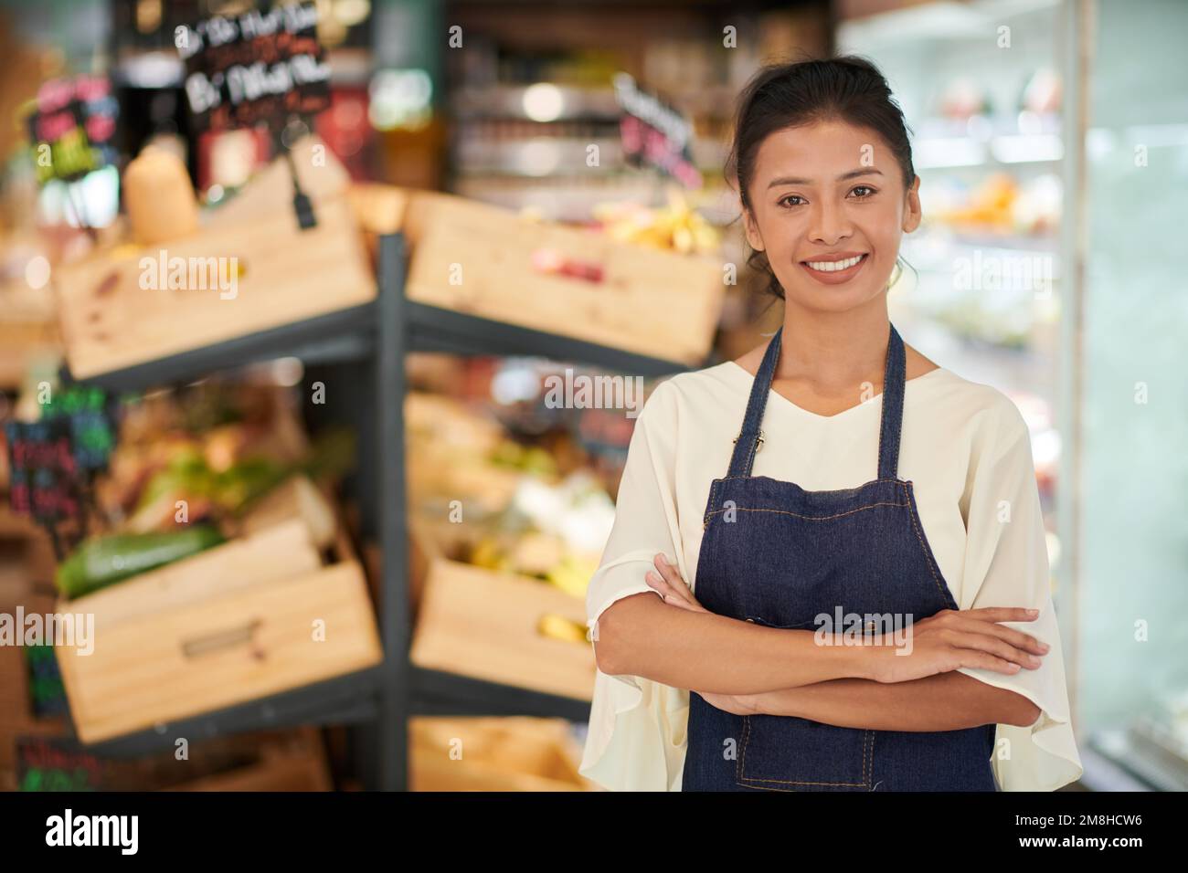 Portrait of smiling grocery store worker standing with her arms crossed ...
