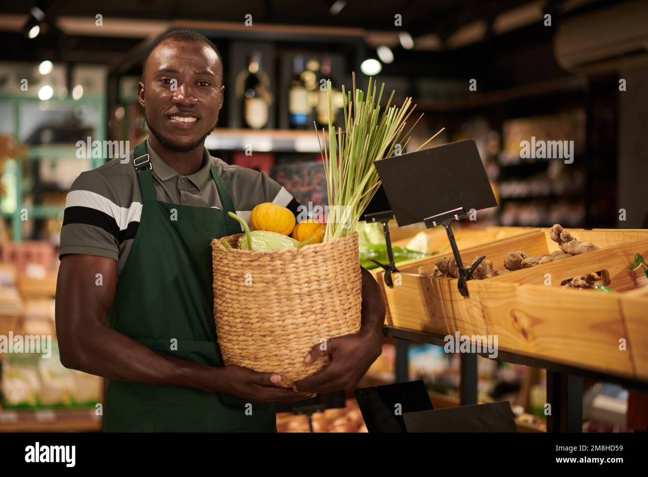 Portrait of smiling grocery store worker with basket of fresh fruits ...