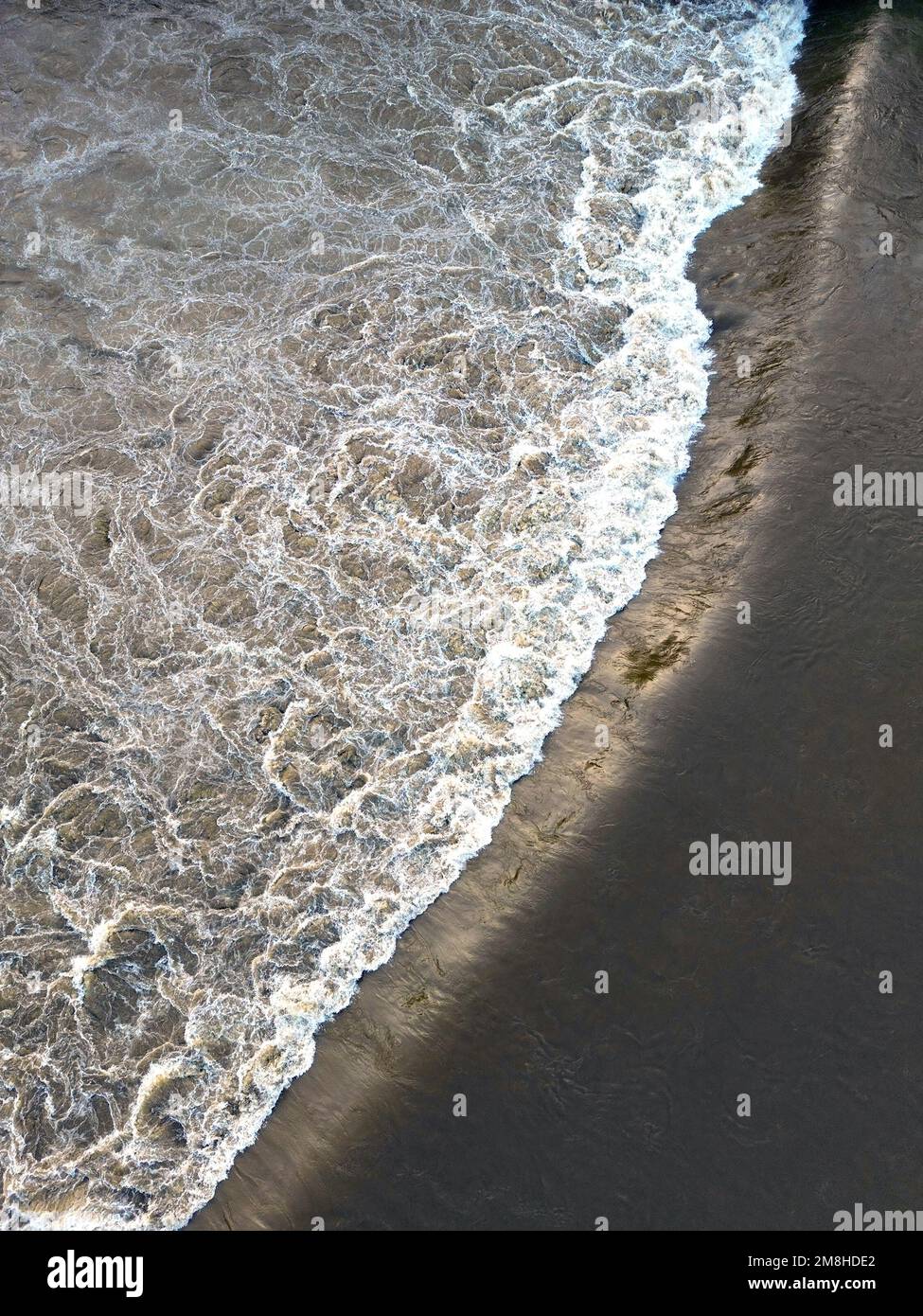 Overhead view of floodwater flowing over a large weir on a river. No ...