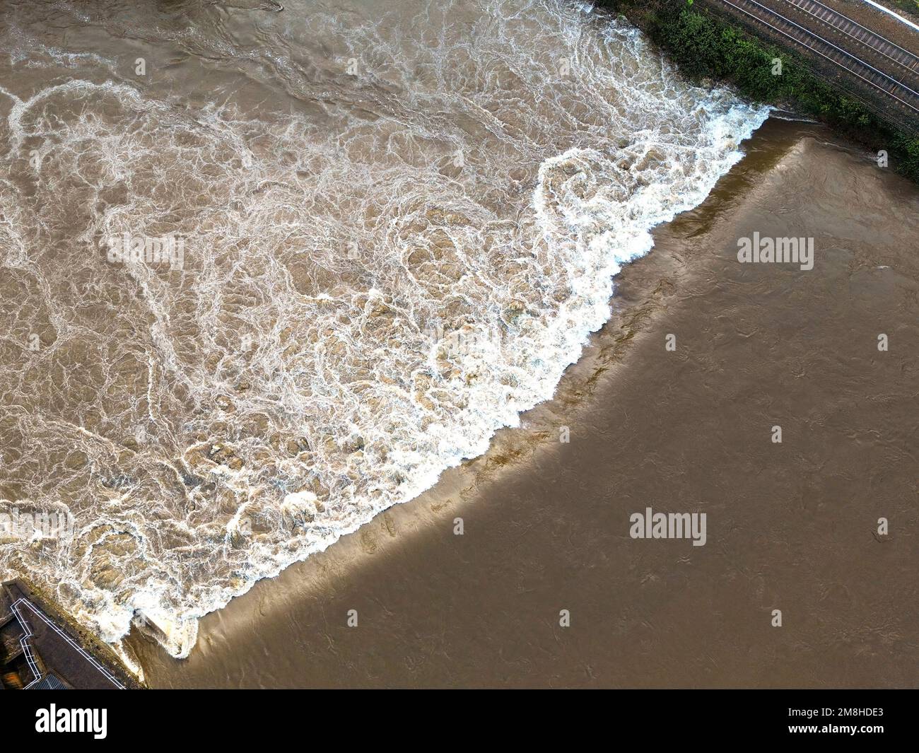 Aerial view of floodwater flowing over a large weir on a river. No ...