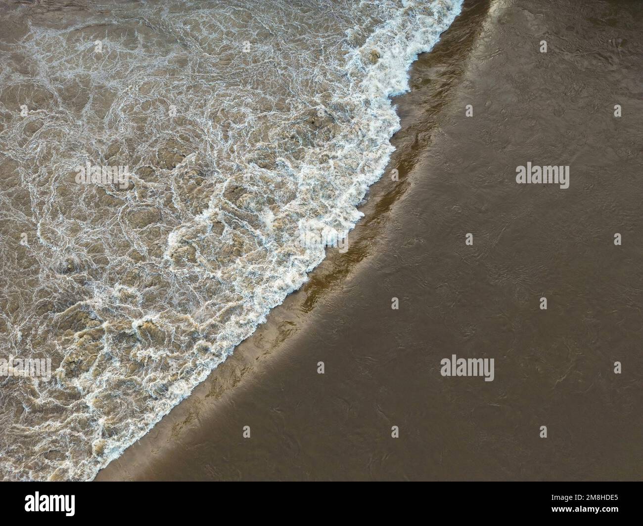 Aerial view of floodwater flowing over a large weir on a river. No ...