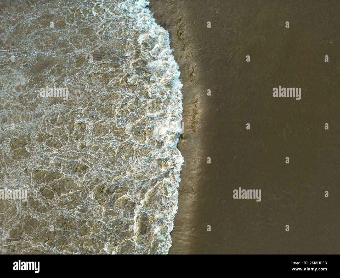 Aerial view of floodwater flowing over a large weir on a river. No ...