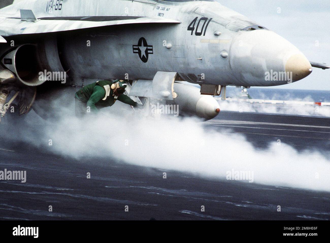 A catapult crewman checks the nose gear of a Fighter Attack Squadron 86 ...