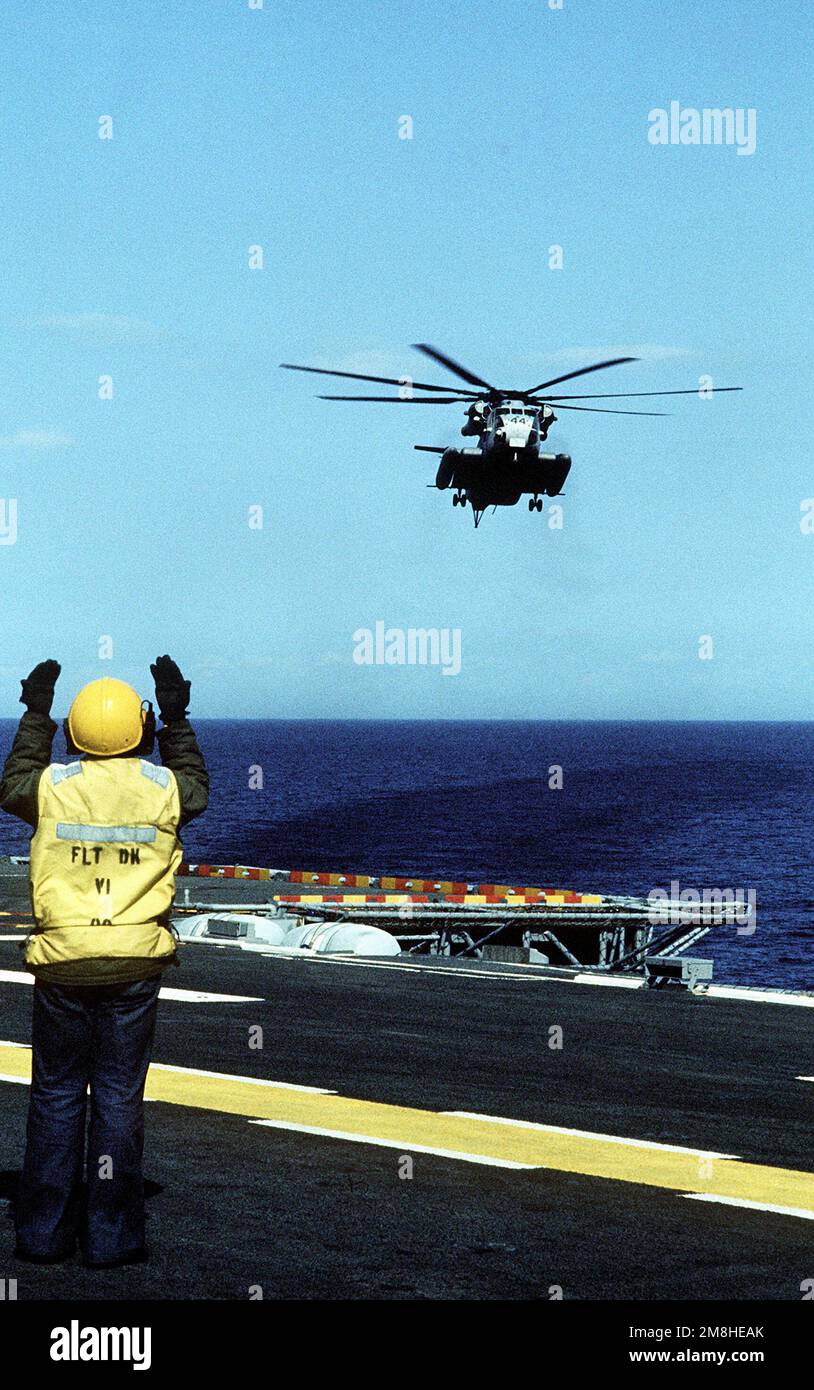 A plane director guides a CH-53E Super Stallion helicopter in for a ...