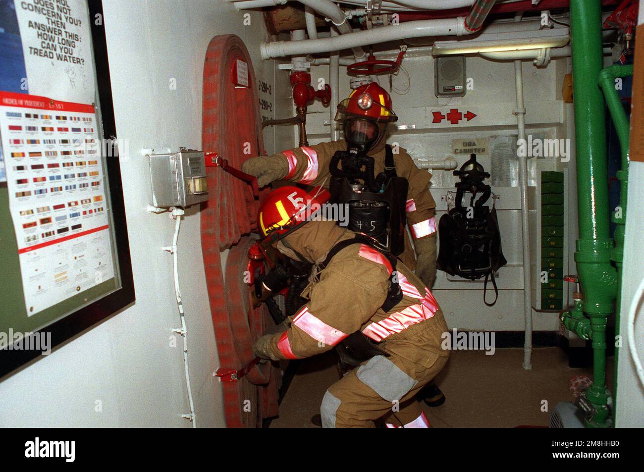 Crewmen wearing oxygen breathing apparatus remove a fire hose from a ...