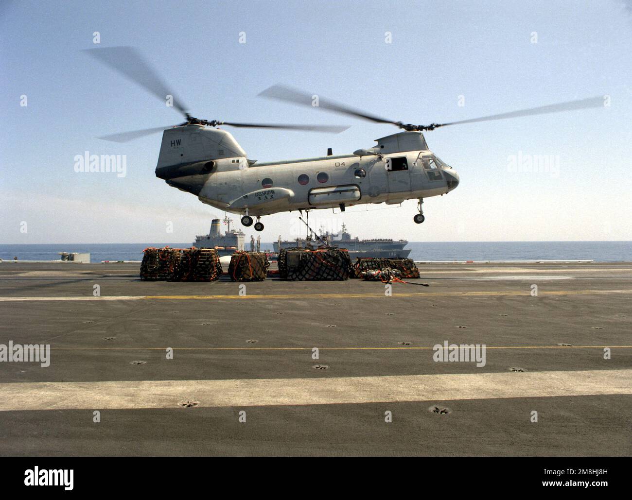 A flight deck crewman attaches a sling to the underside of an HH-46D ...