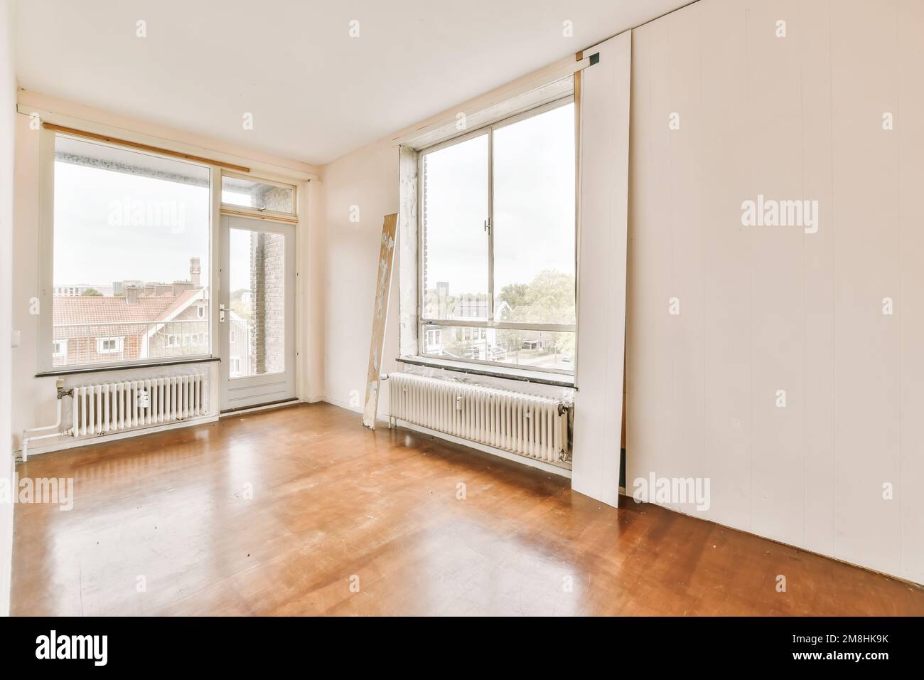 an empty living room with wood flooring and large windows looking out ...