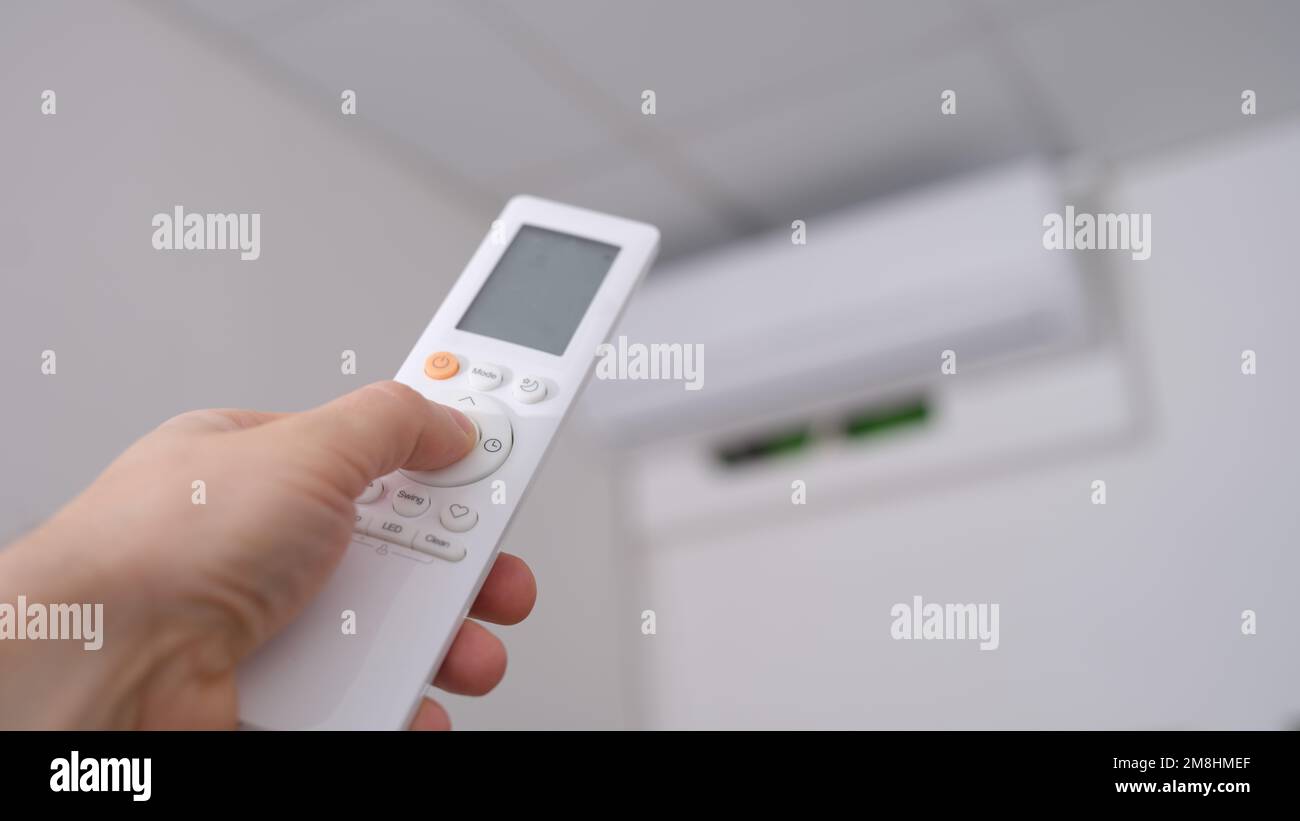 Woman hand holds remote control pointing at air conditioner in room ...