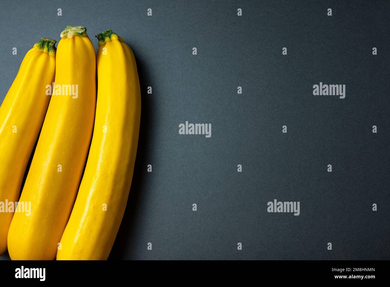 three yellow courgettes on dark grey background Stock Photo - Alamy