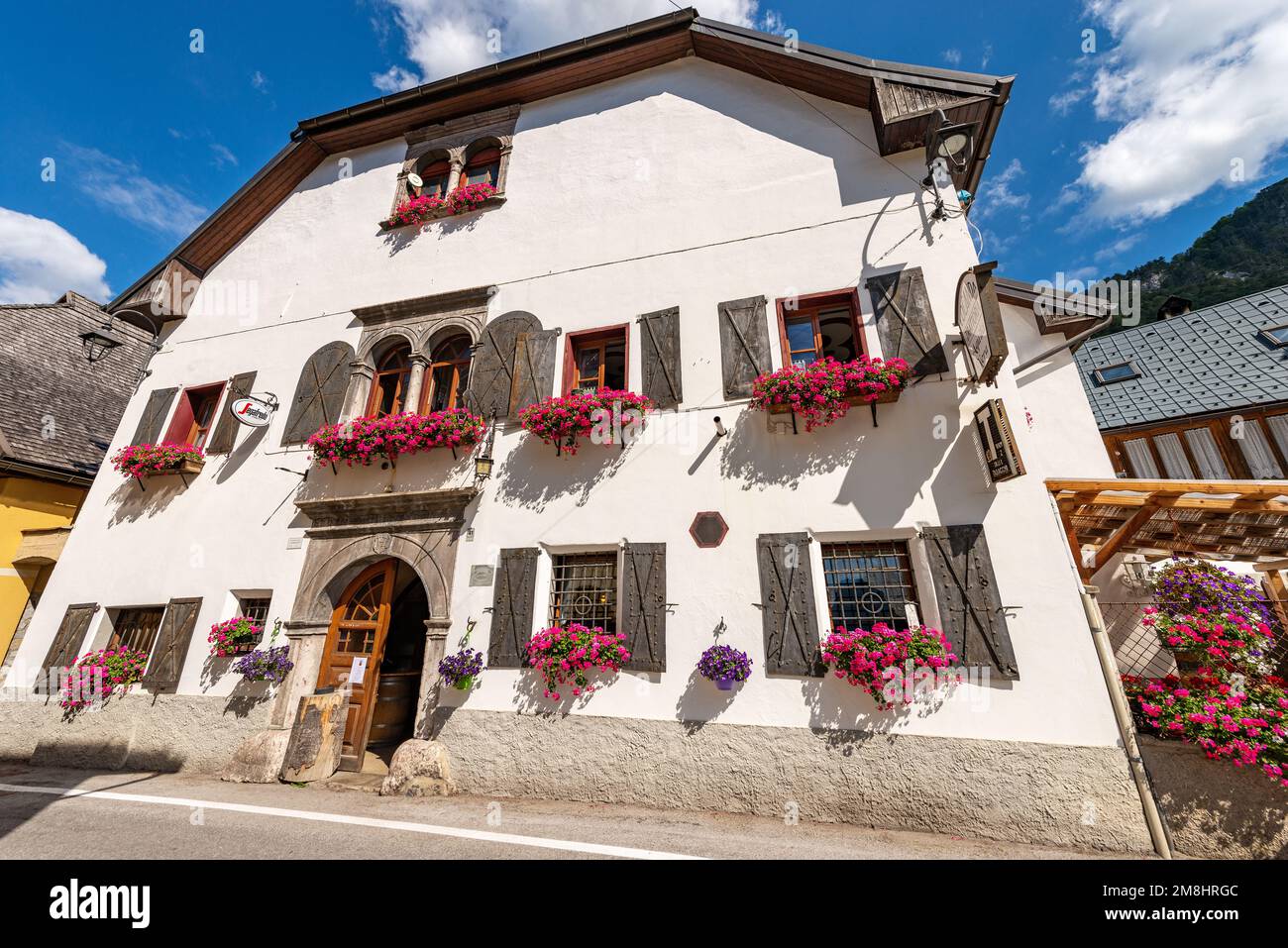 Building with windows with metal shutters and geranium flowers. Village ...
