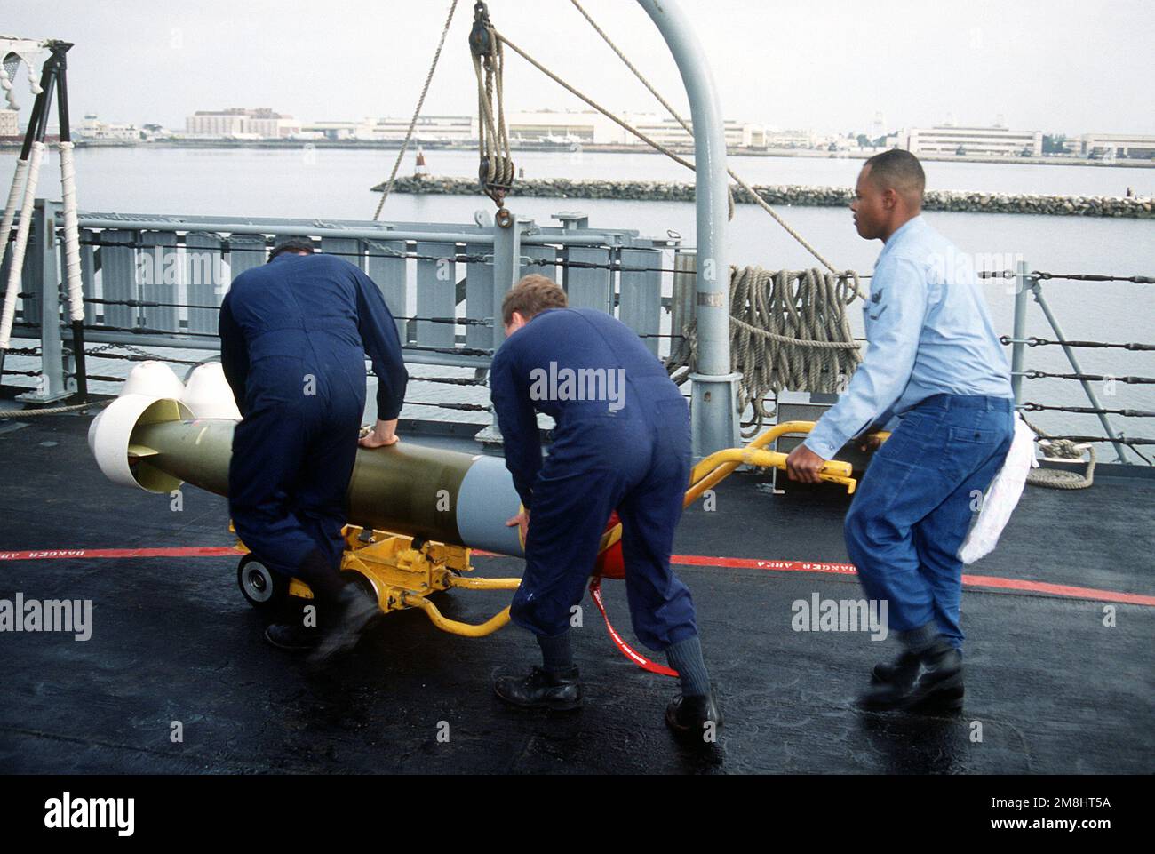 Members of the Weapons Division push a Mark 46 torpedo across the deck ...