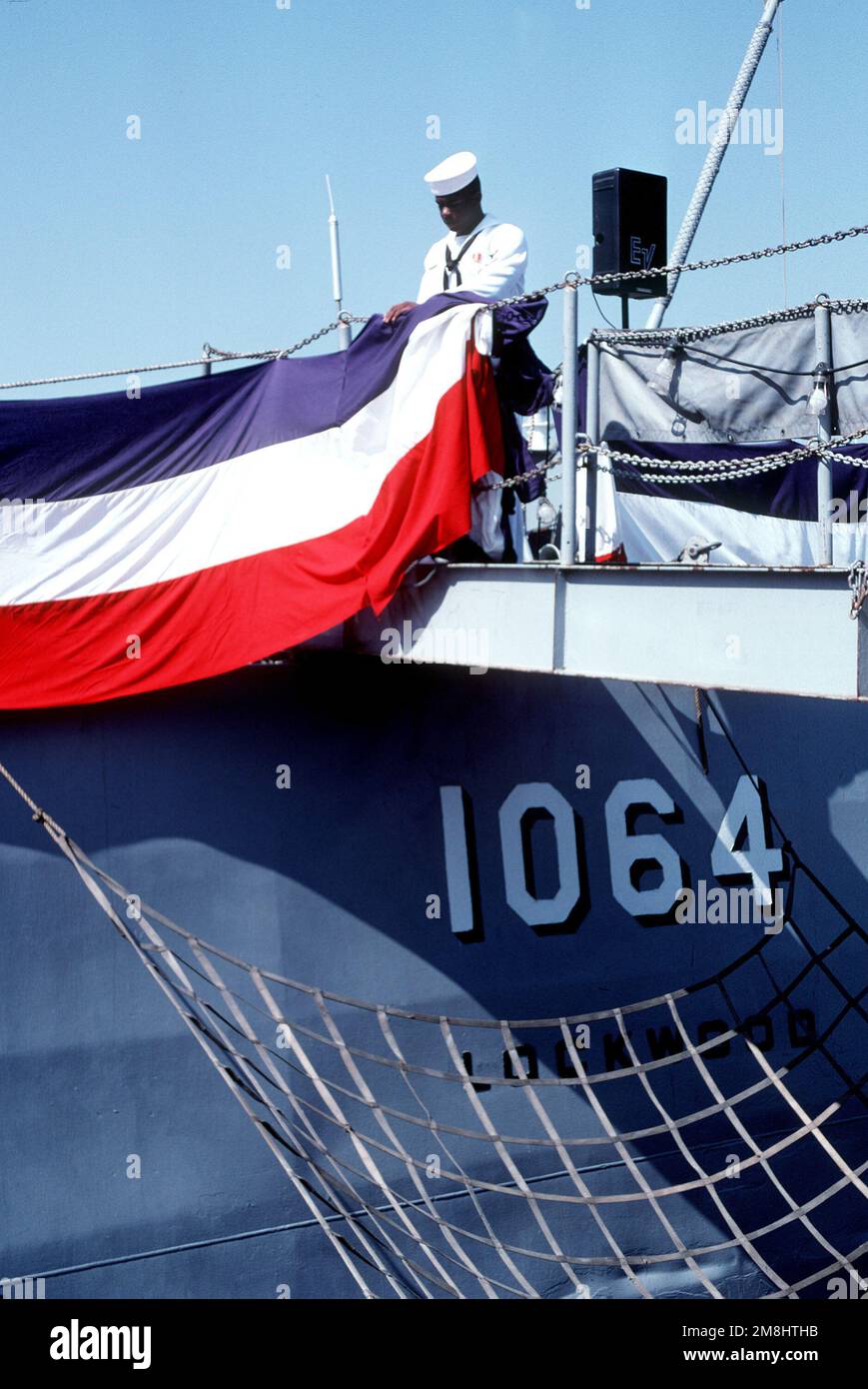 A sailor adjusts the bunting on the bow of the frigate USS LOCKWOOD (FF ...