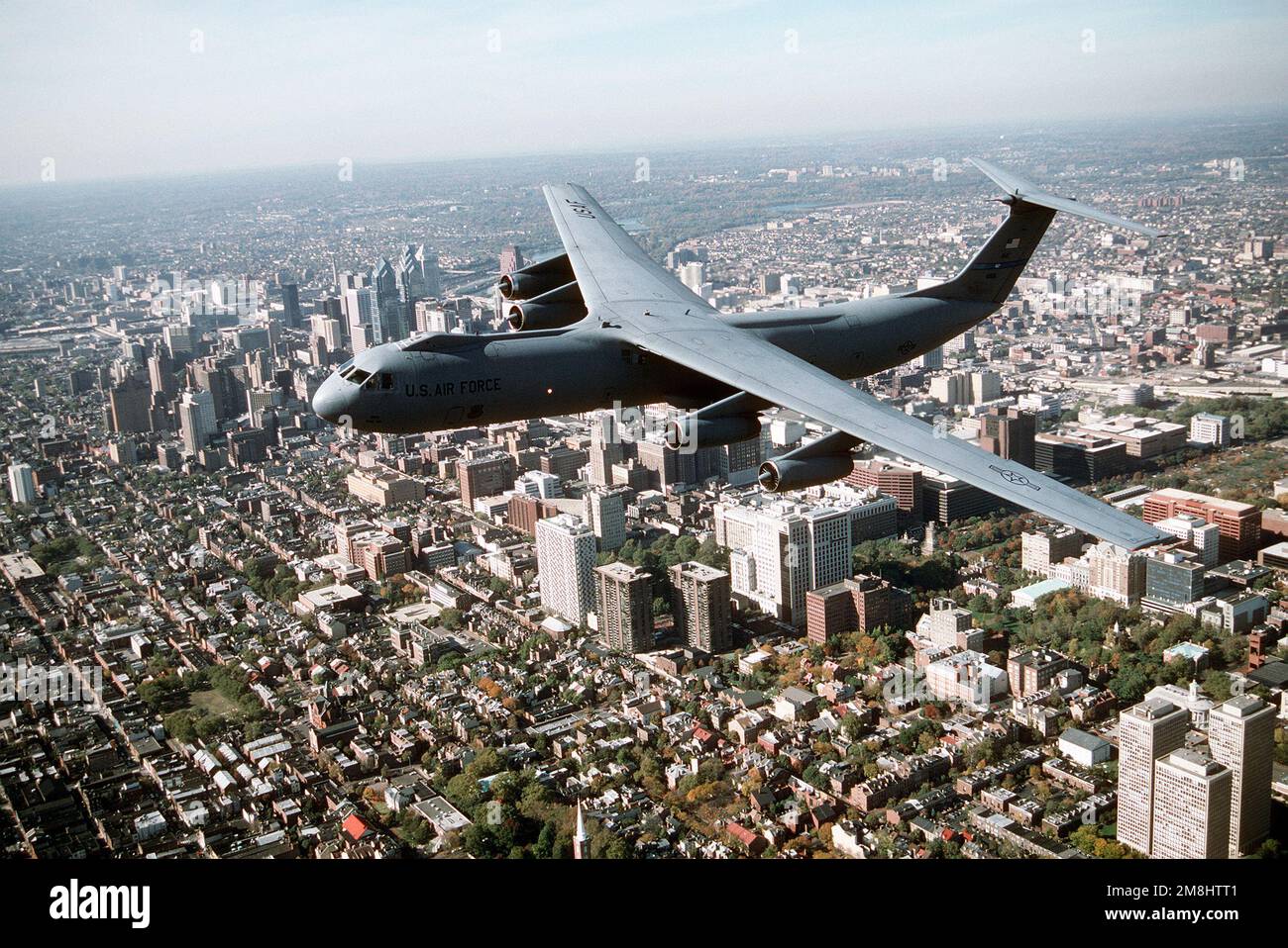 An air-to-air left side view of a 438th Airlift Wing, C-141 Starlifter flying over downtown area ...